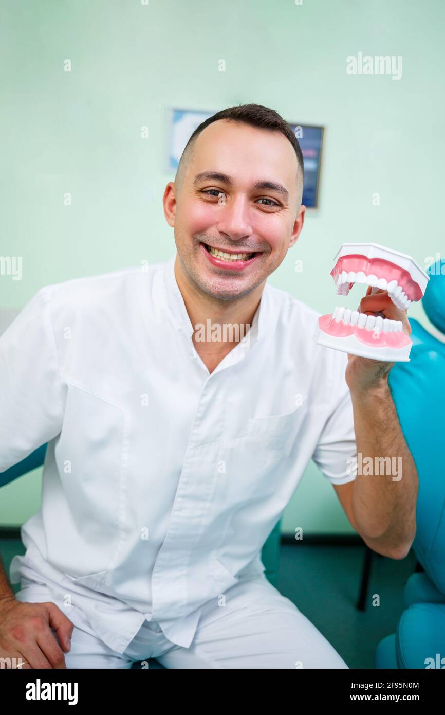 Positive doctor in white uniform showing mock jaw with teeth while ...