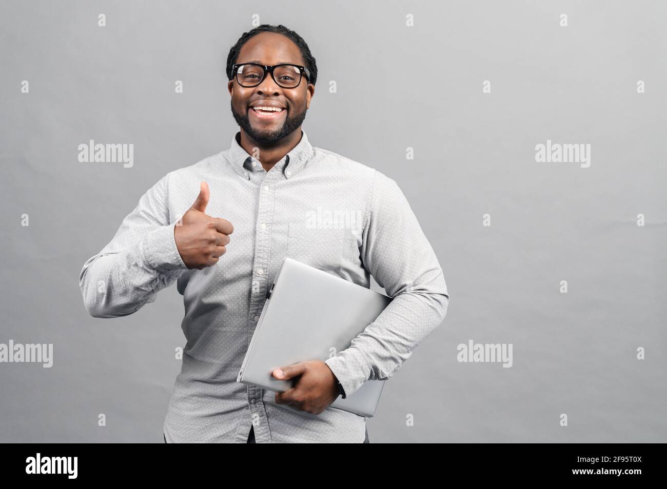 Cheerful African-American man carrying laptop computer isolated on grey ...