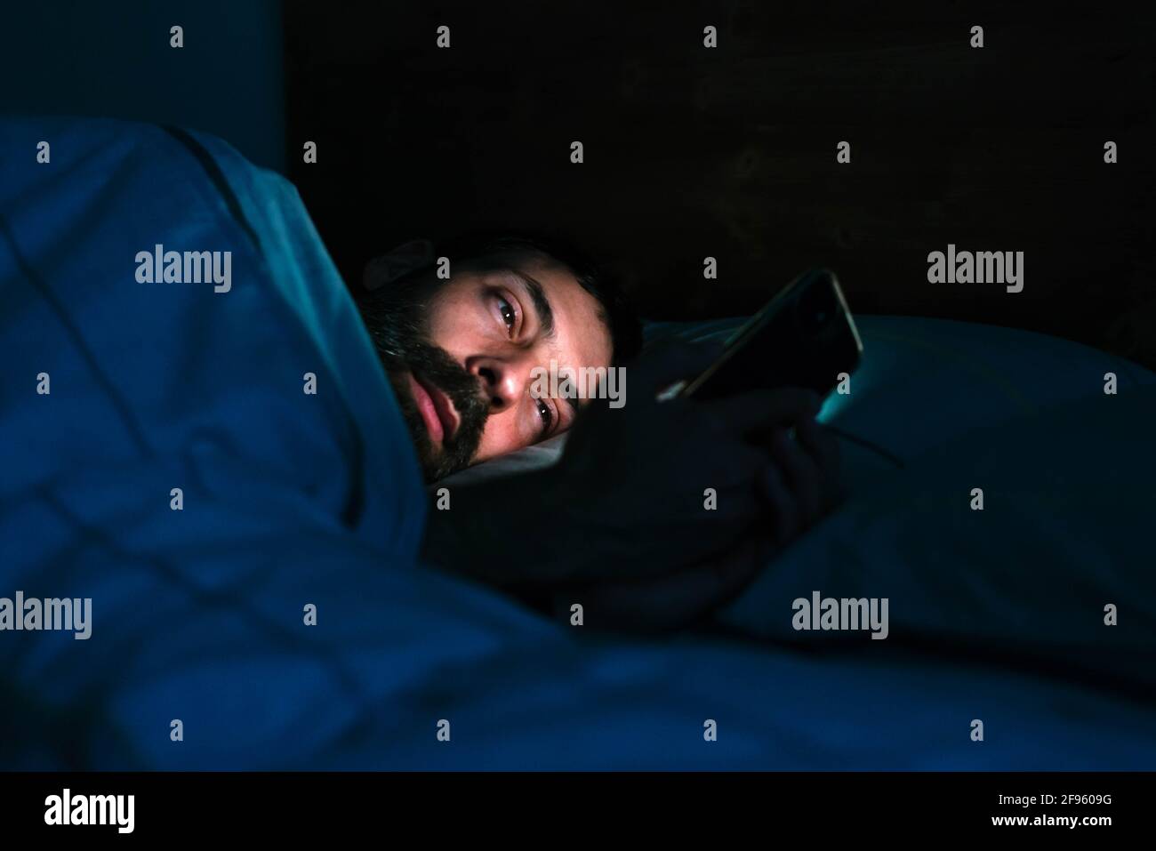 Young man lying in bed and using mobile phone Stock Photo - Alamy
