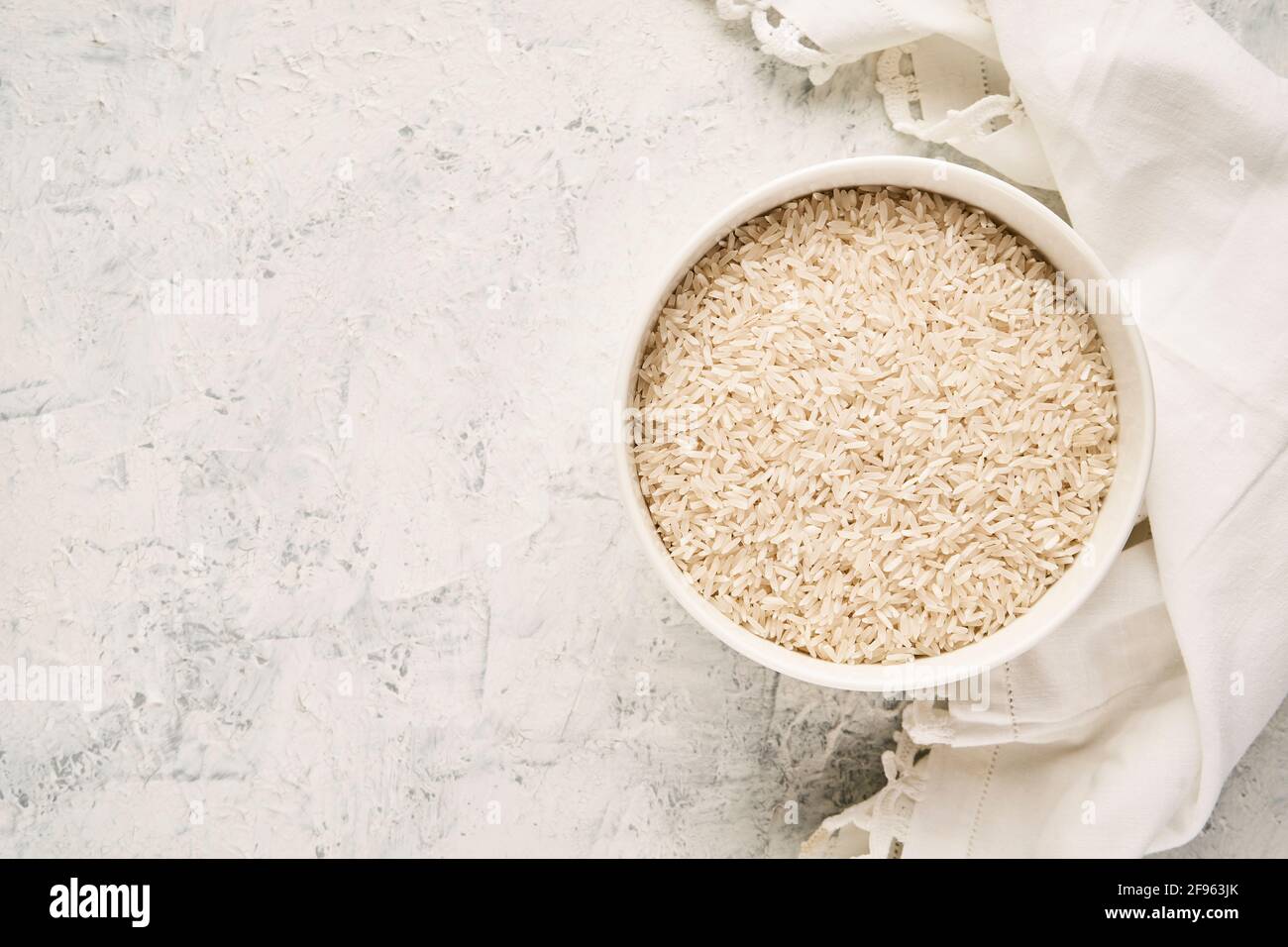 Top view of a bowl filled with raw white rice on a textured background ...