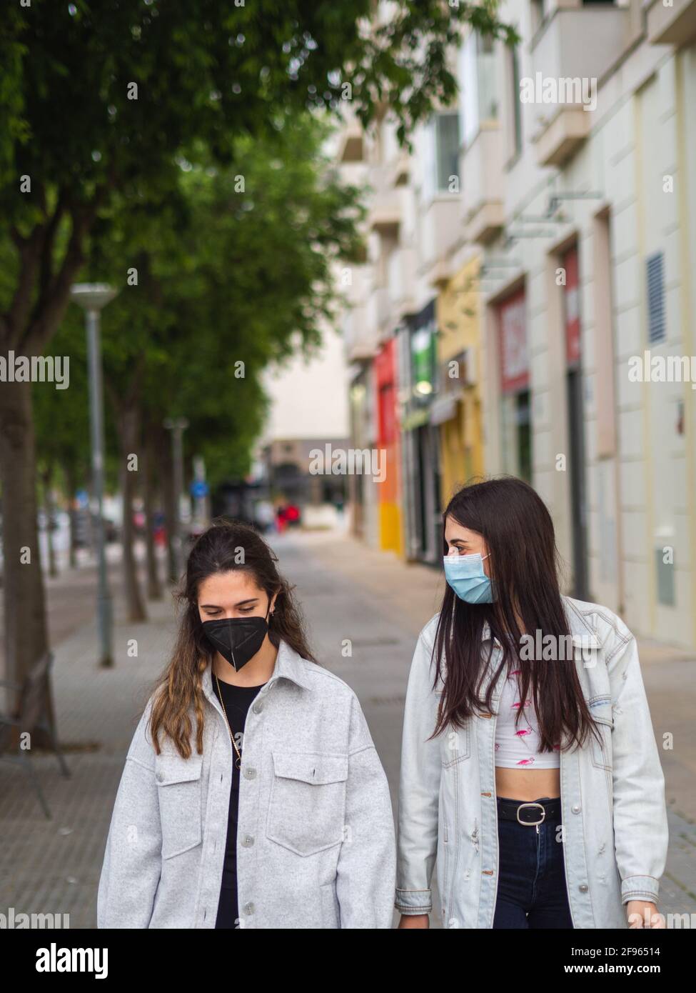 Shot of two Caucasian girls from Spain in masks walking on the street ...