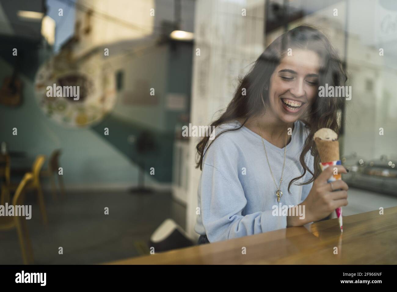 Shot of a happy Caucasian girl eating ice cram in cafe. A shot through ...