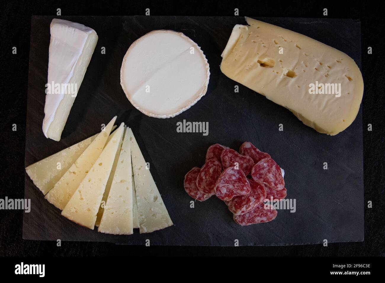 High angle shot of different kinds of cheese and salami on a black ...