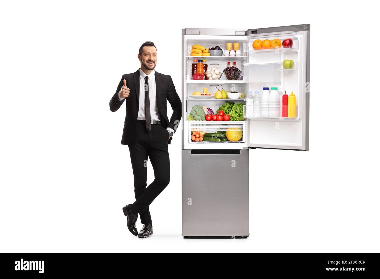 Full length portrait of a young man in a suit leaning on an open fridge ...