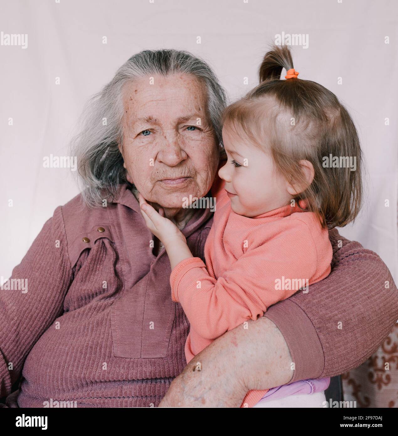 An elderly grandmother holds a beautiful little girl in her wrinkled ...