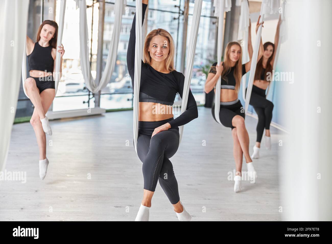 Group of female are doing fly yoga exercises in fitness training white ...