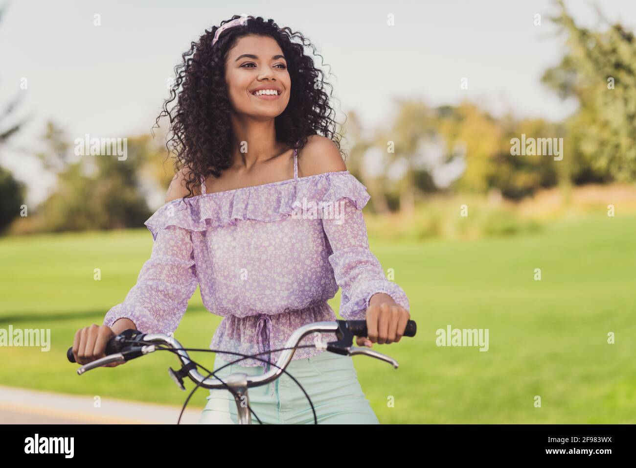 Photo of positive dark skin girl sit on bike look interested far nice ...