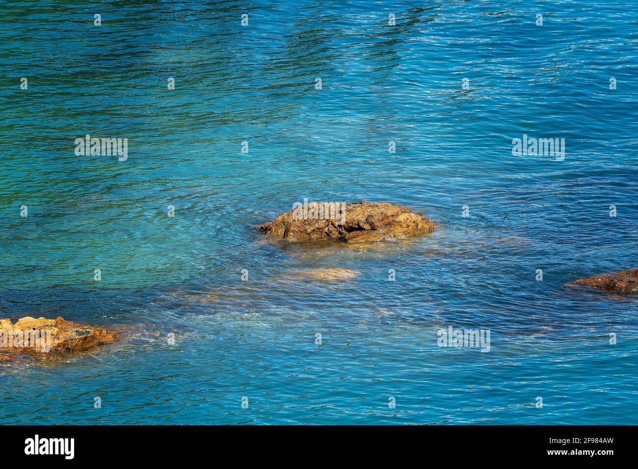 Rocks visible out of the clear blue sea water Stock Photo - Alamy