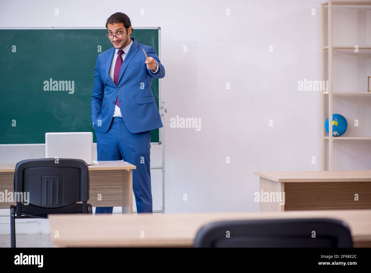 Young teacher in suit in front of green board Stock Photo - Alamy