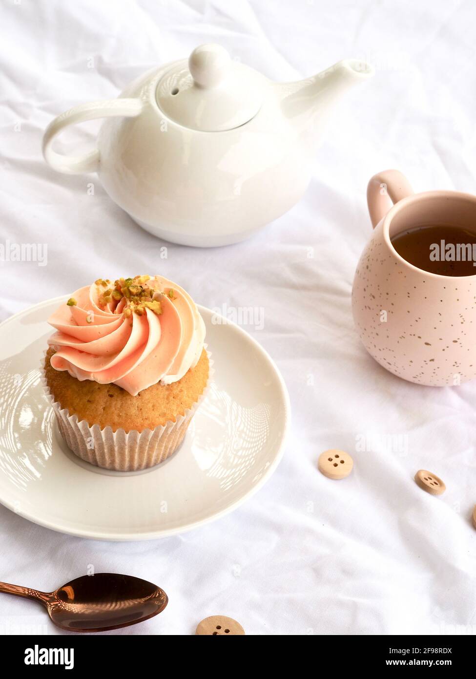 Pretty pink cupcake, pink mug and white teapot on a white pretty ...