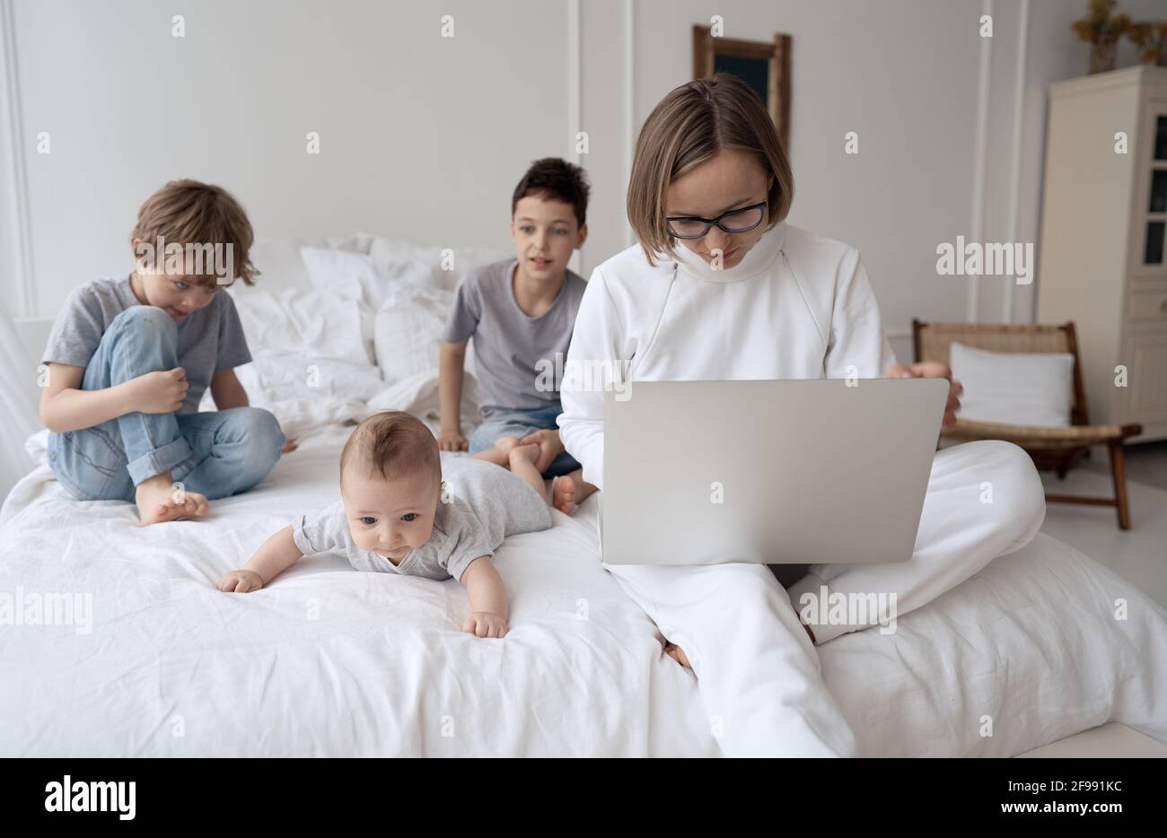 Busy caucasian woman trying to work while baby sitting three kids ...