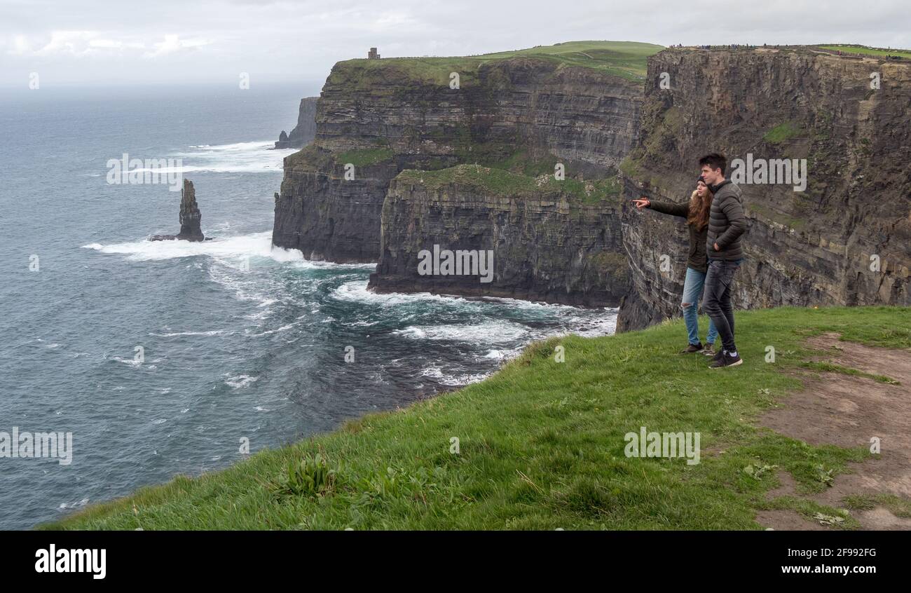 Young couple stands at the edge of the steep Cliffs of Moher in Ireland ...