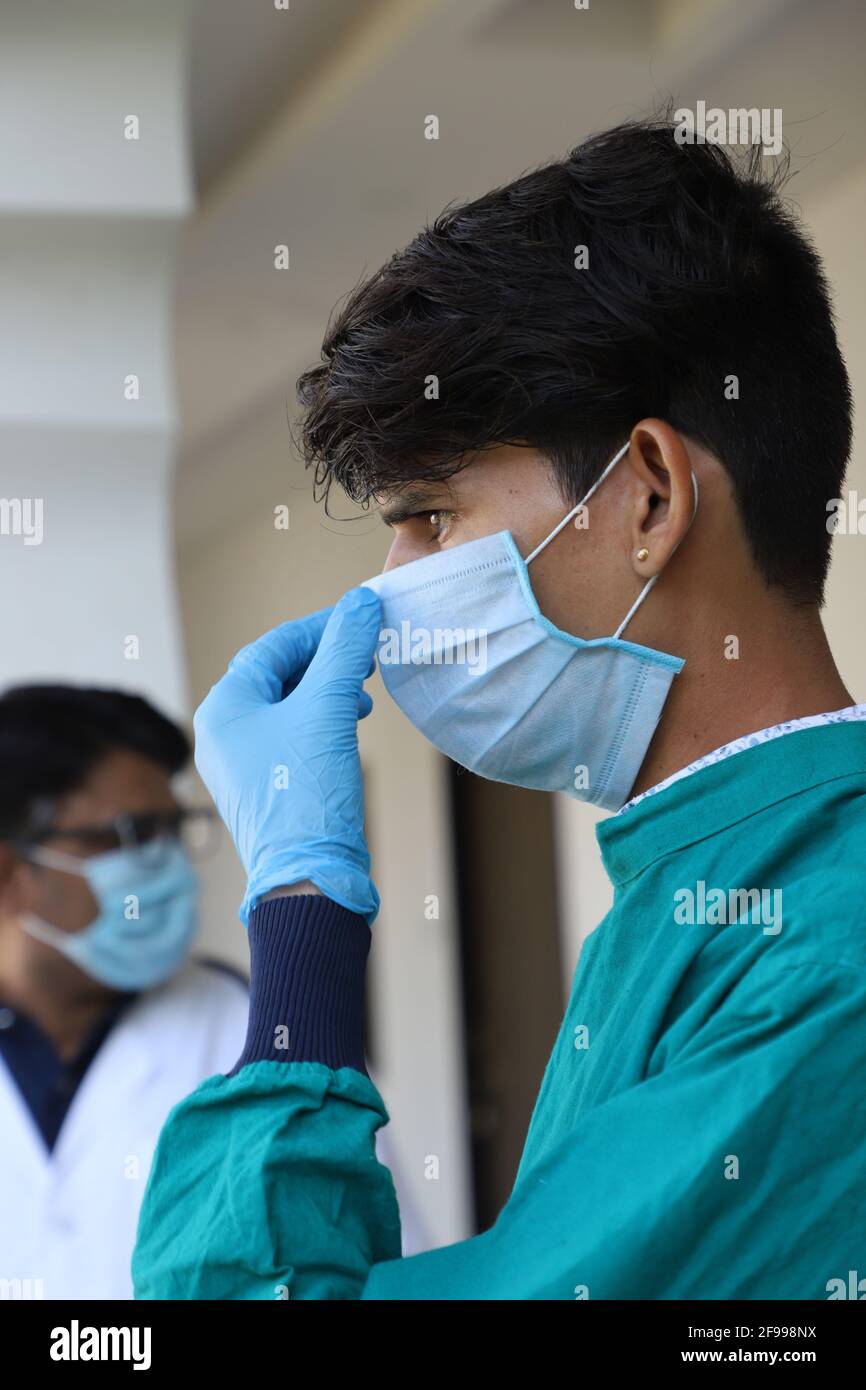 Side view of a male nurse with a medical uniform fixing his face mask ...