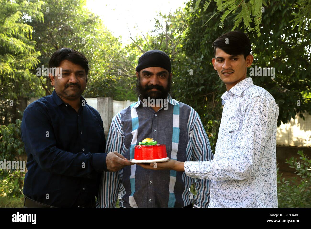 Front view of three happy Indian men holding an orange Jelly cake ...