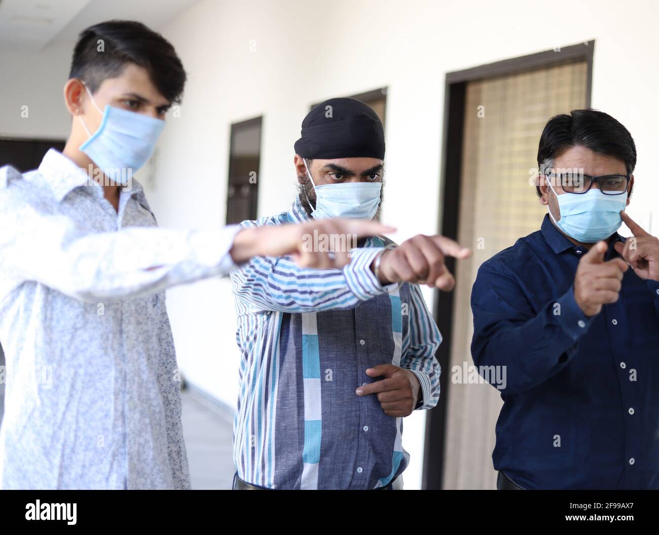 Side view of three Indian men wearing face masks pointing at something ...