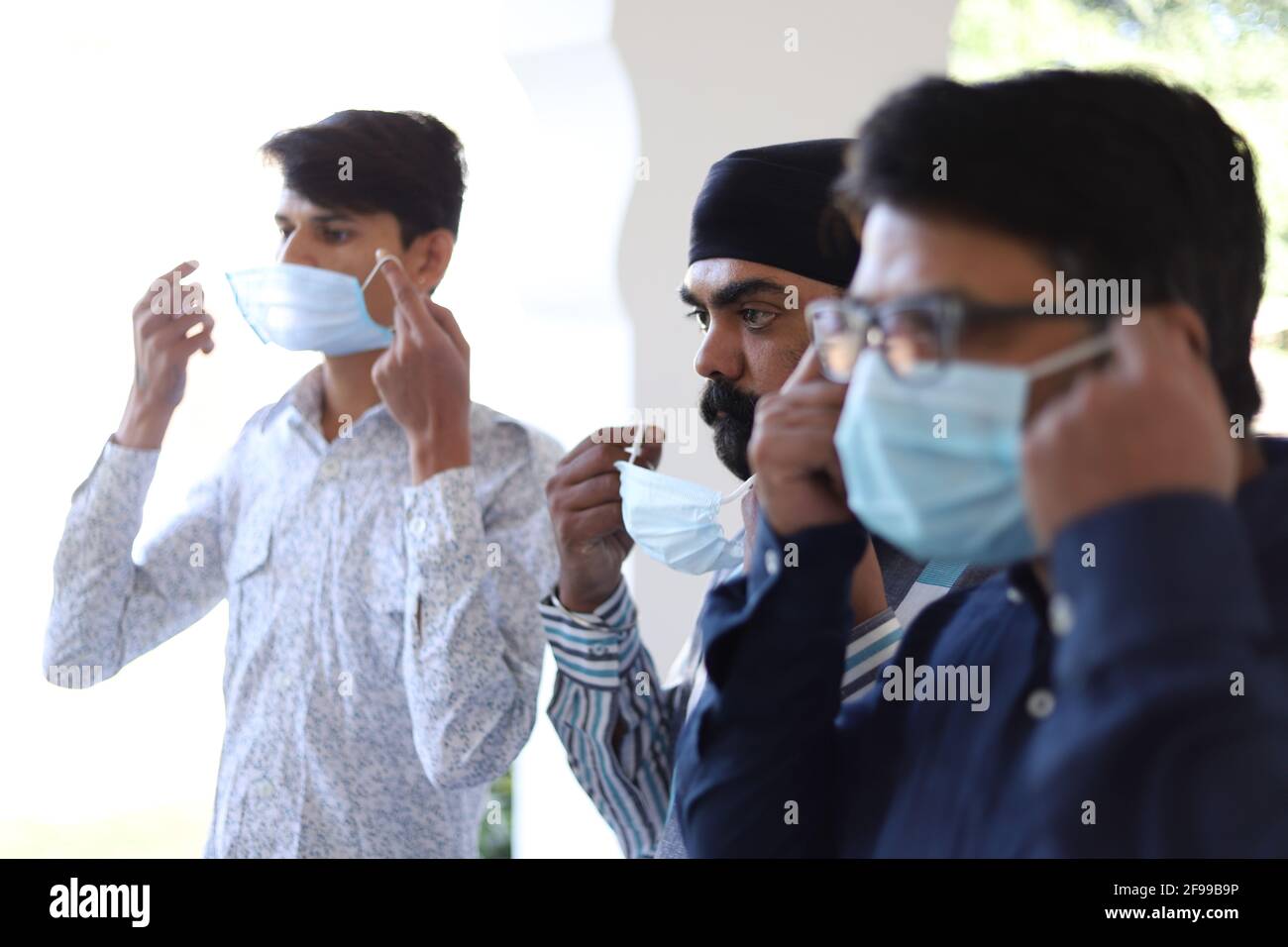 Side view of three Indian men putting on their face masks standing ...