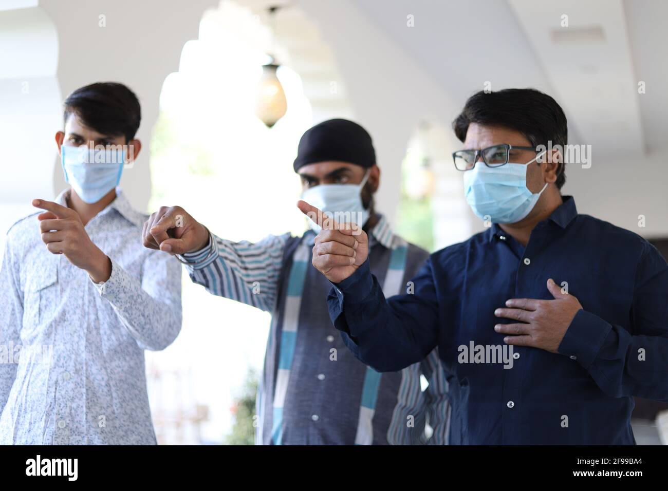Front view of three Indian men wearing face masks pointing at something ...