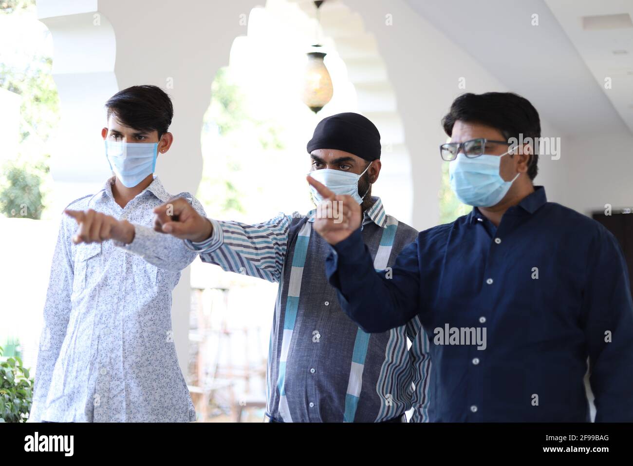 Front view of three Indian men wearing face masks pointing at something ...
