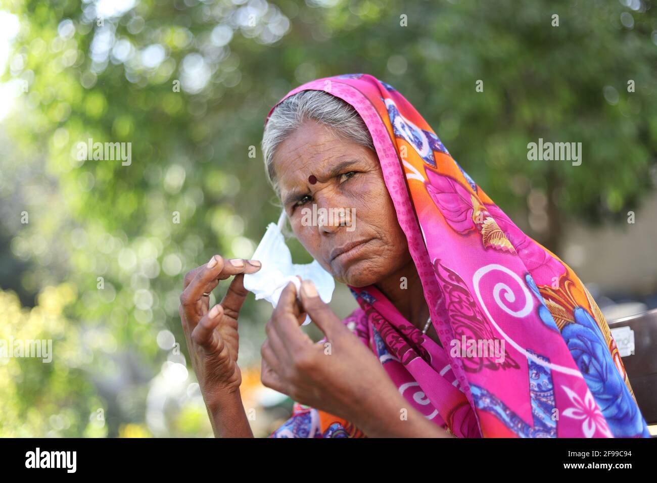 Indian woman wearing a colorful sari and putting on a protective mask ...