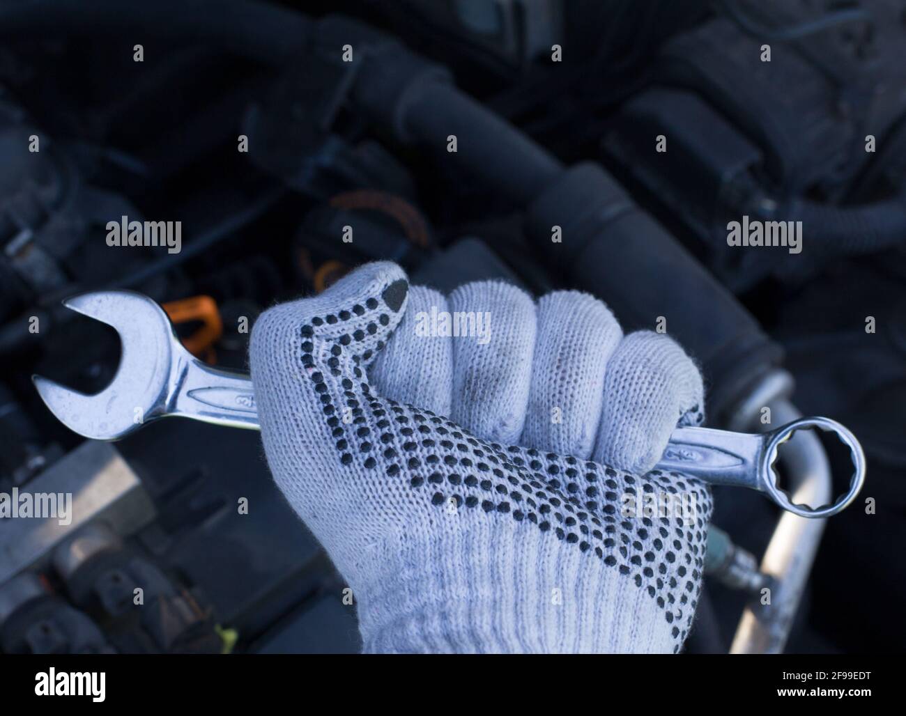 Car mechanic working on a car engine in the workshop - holding a tool ...