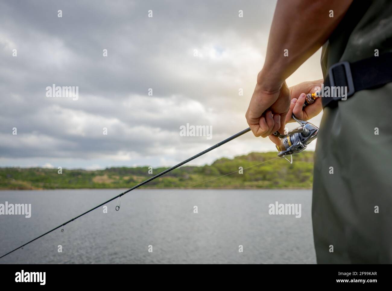 A wading fisherman, with rod and reel, tries to catch a fish in the ...