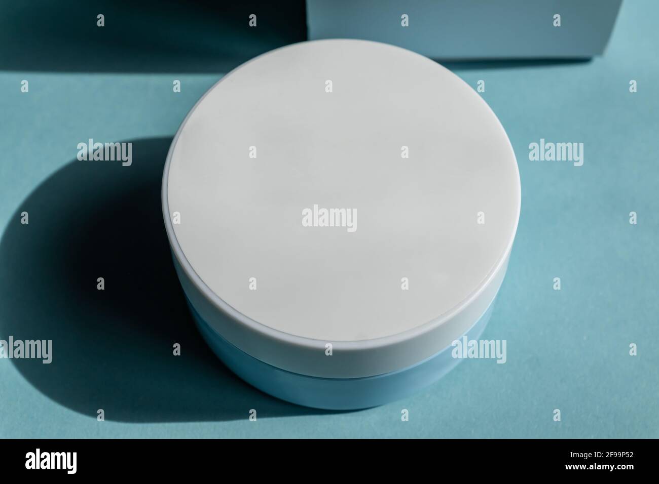 Face cream jar with plastic cap and whire carton box, package on blue ...