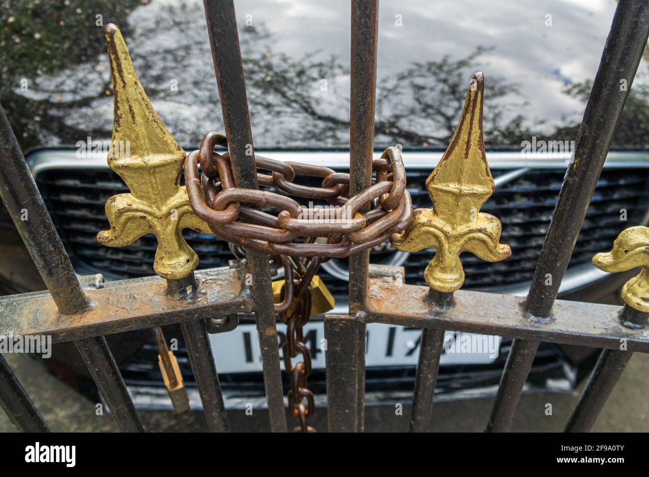 A luxury black car parked behing metal gates locked with a chain and ...