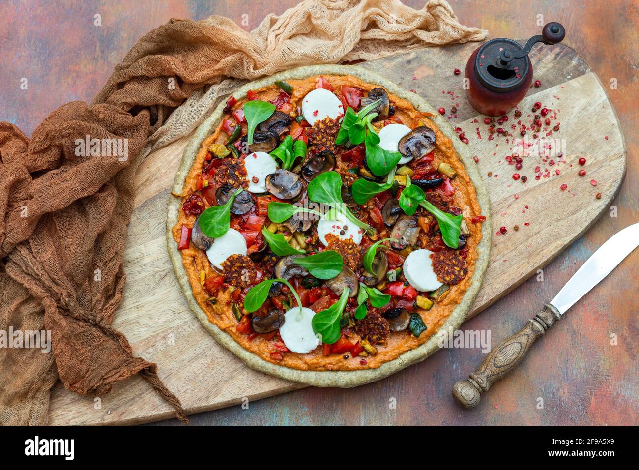 Top view of raw vegan pizza next to an old red pepper mill with dried ...