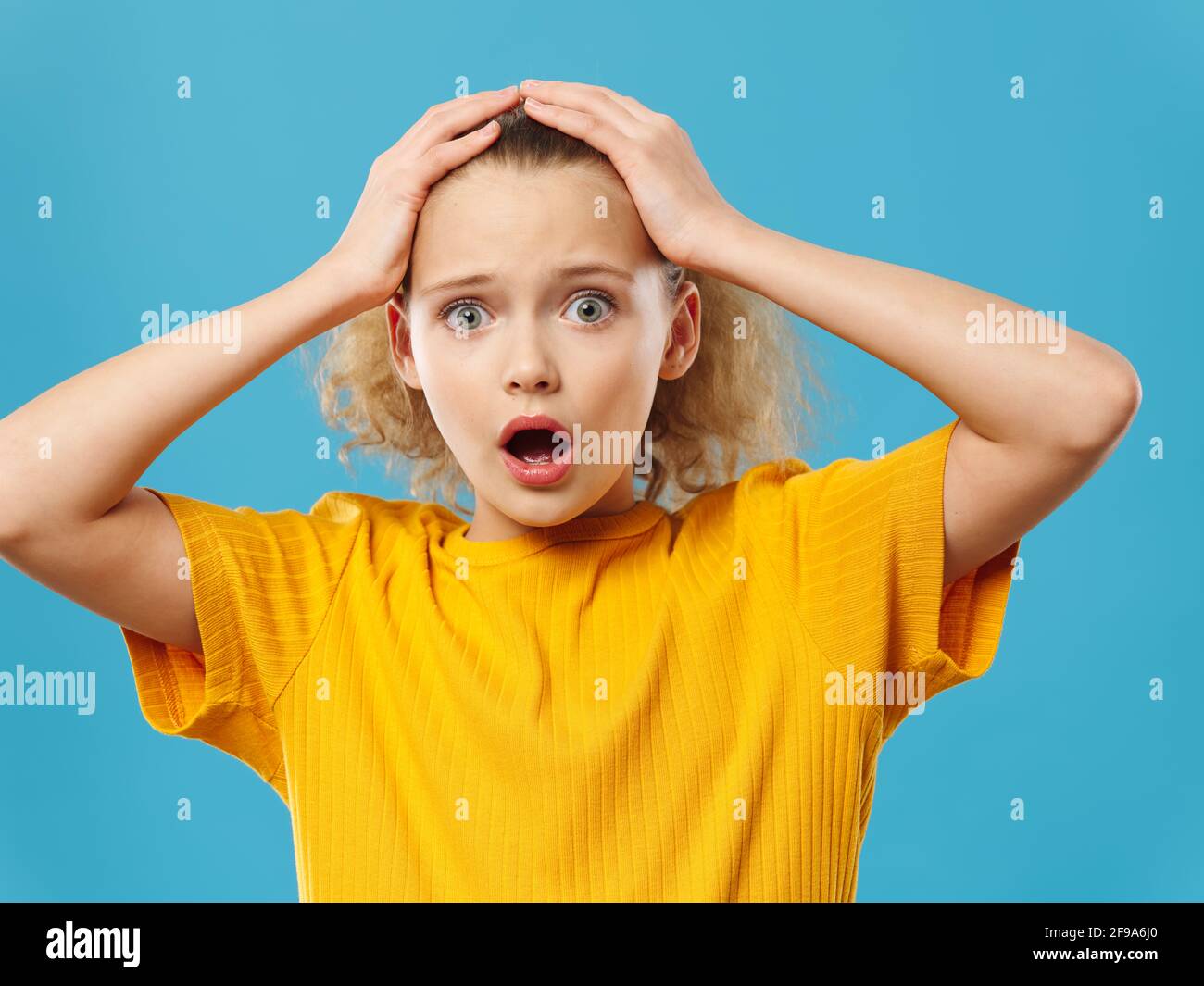 girl with curly hair emotion yellow t-shirt blue background Stock Photo ...