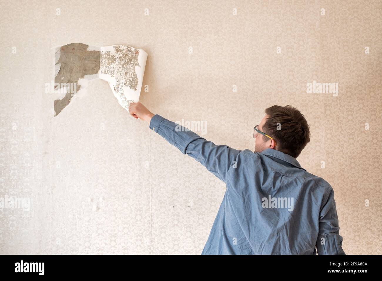 Process of flat renovation. Caucasian man tearing off old wallpaper ...