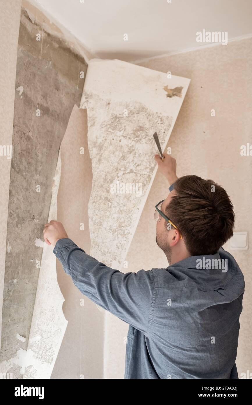 Process of flat renovation. Caucasian man tearing off old wallpaper ...