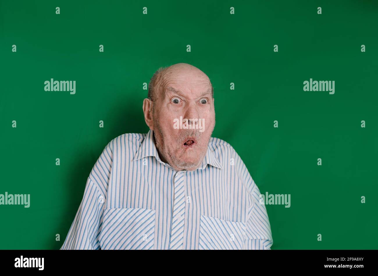 a crazy old man makes faces and grimaces against an isolated green ...