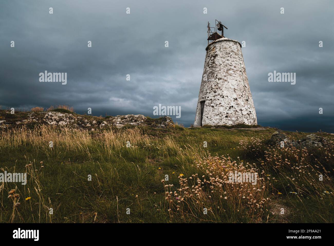 Small stone tower in front of a dramatic cloudy sky on Ynys Llanddwyn ...