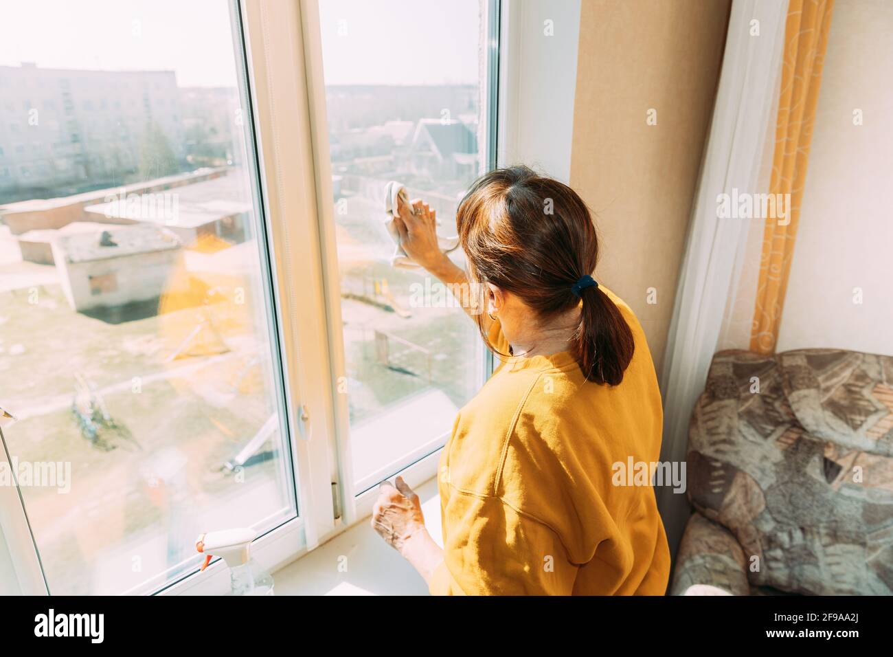 Woman Of Fifty In Yellow Sweater And Jeans Washes Dusty Window In ...