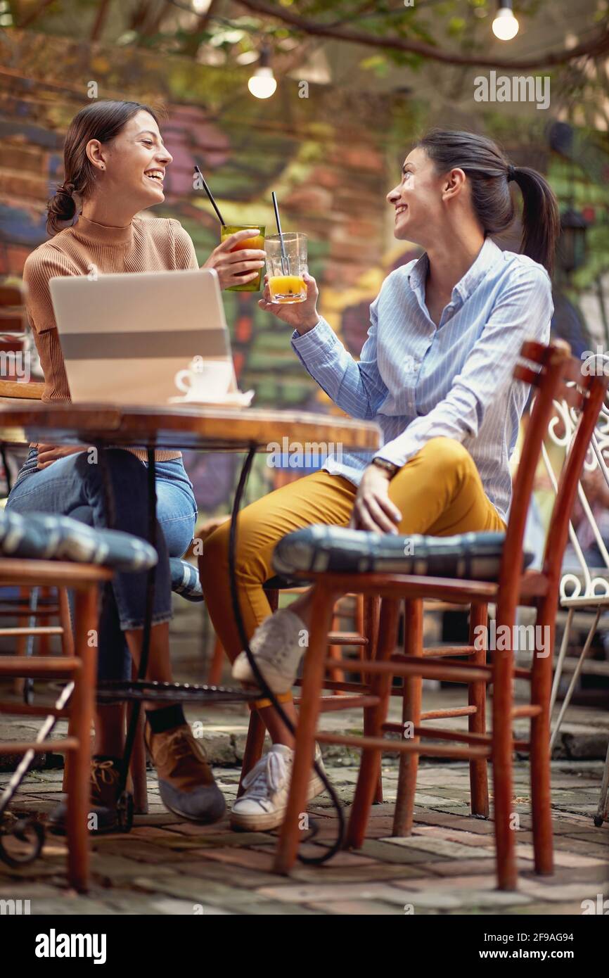 Two female friends toasting while having a drink in a cheerful ...
