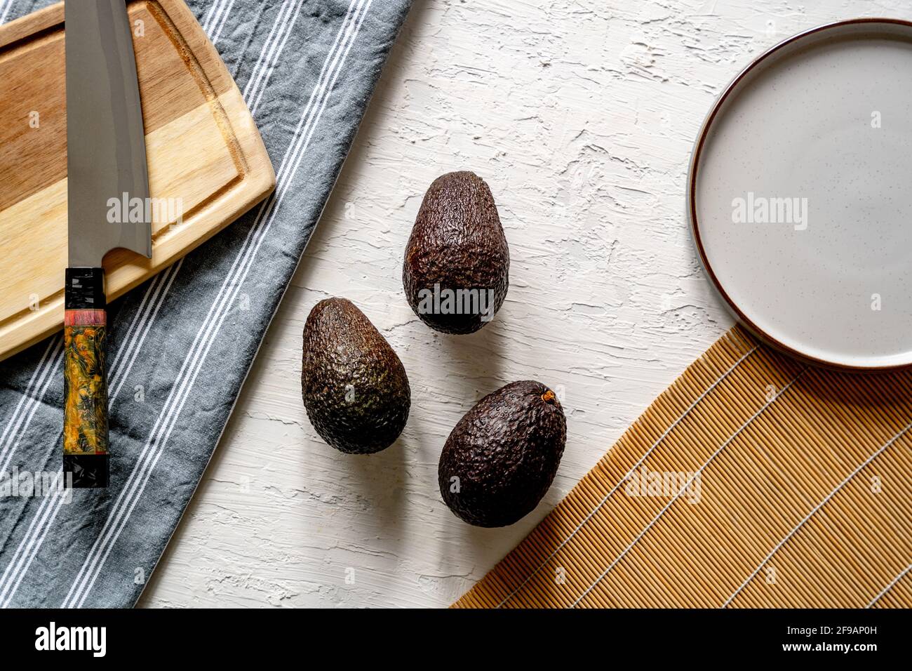 Top view of three whole avocados, a cutting board, a sharp knife, and a ...