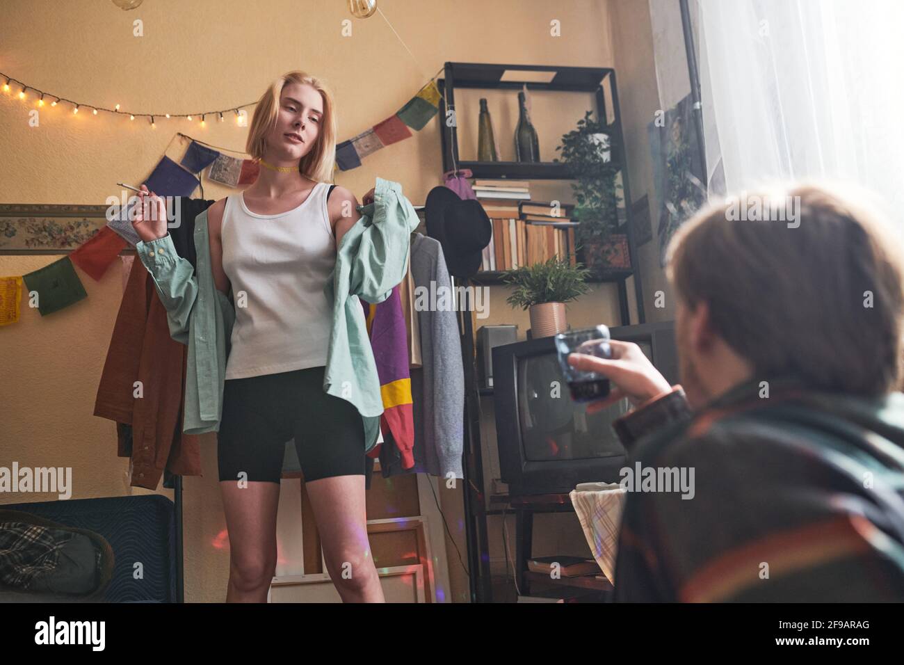 Young woman smoking a cigarette and dancing with young man sitting and ...