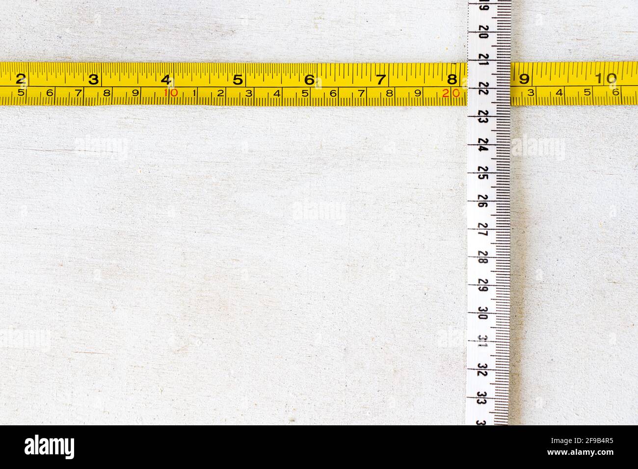 Yellow measuring tape and metal ruler crossing each other on a white ...