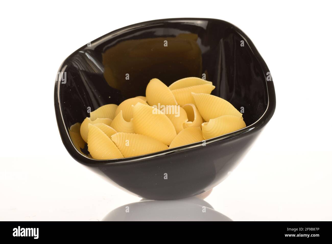 Several bright yellow, organic, uncooked shell-shaped pasta in a black ...