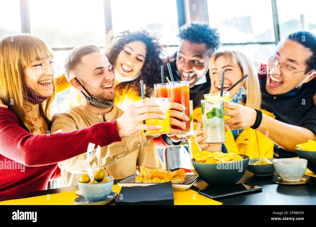 Multiracial friends wearing face masks drinking cocktails at bar ...