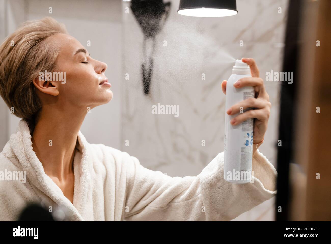 Smiling young woman spraying her face with a thermal water while ...
