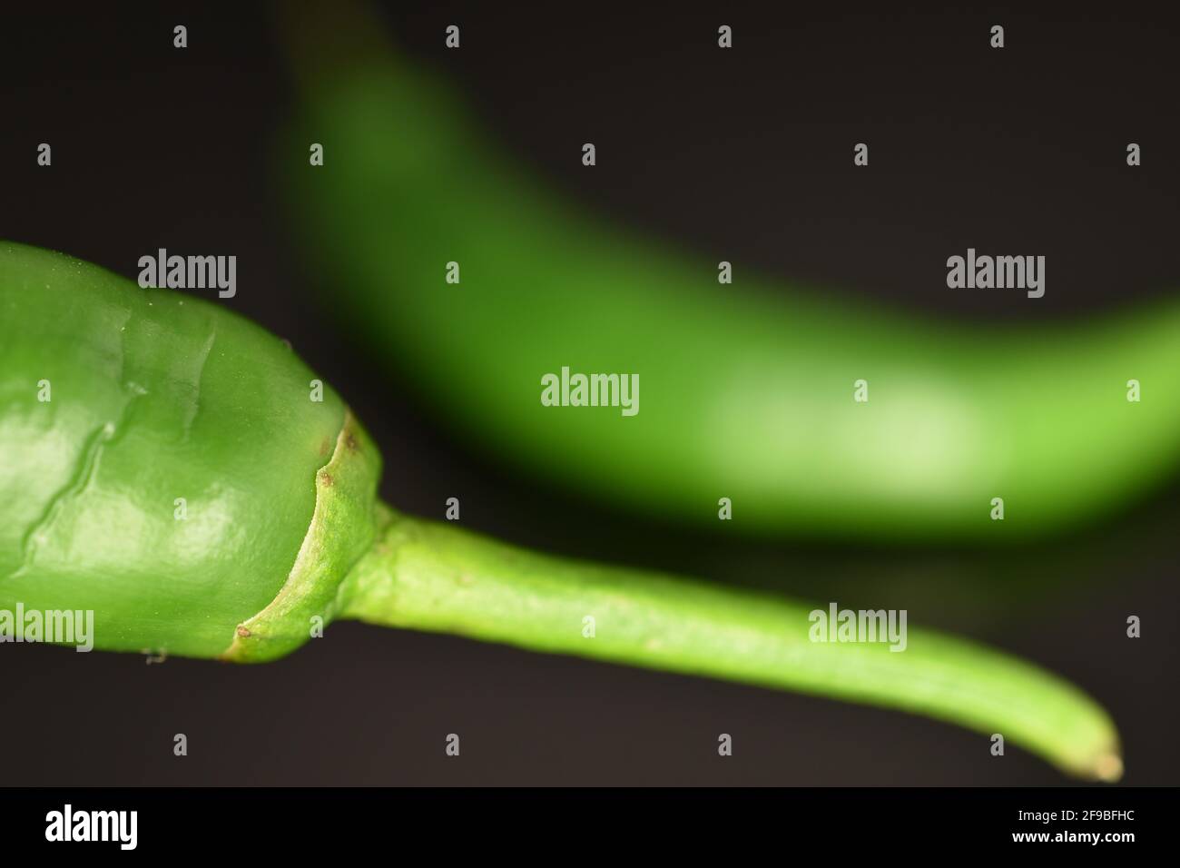 Two dark green organic, natural, spicy, hot pepper pods on a black ...