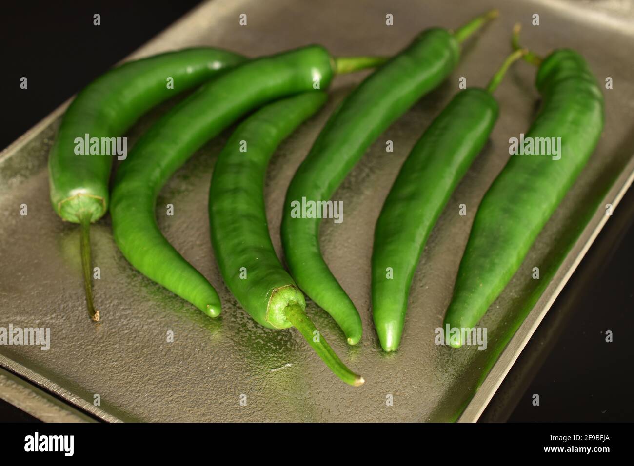 A few dark green organic, natural, spicy, hot pepper pods on a metal ...
