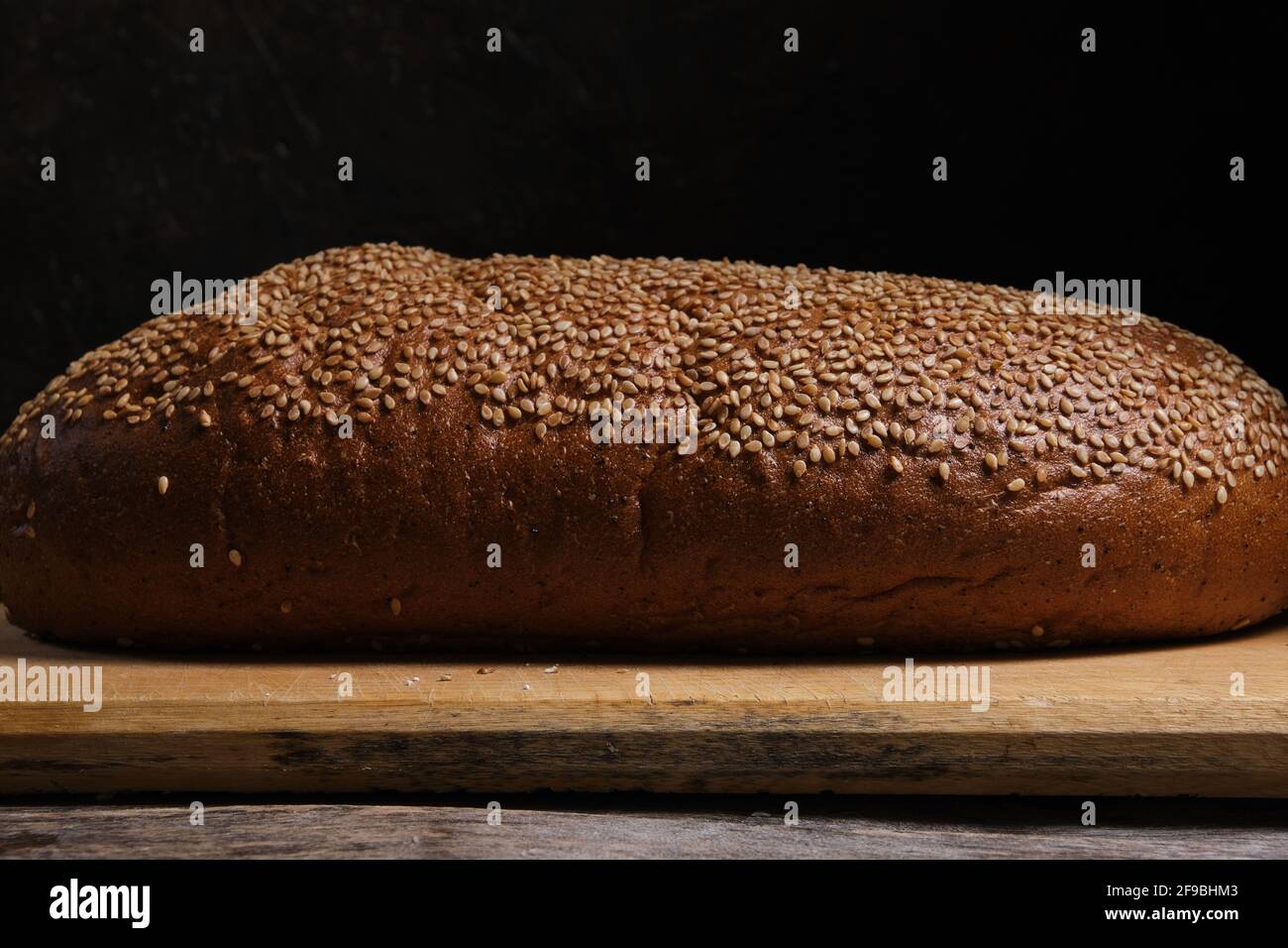 Bun lies on cutting board sprinkled with sesame seeds on dark ...