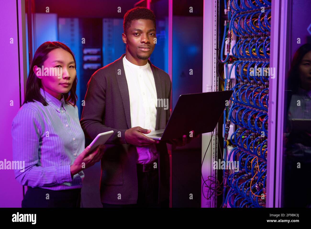 Portrait of confident multi-ethnic IT engineers standing with gadgets ...