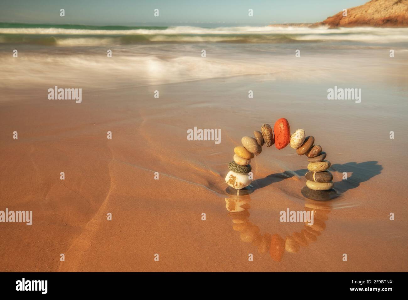 Creative stone arch with red stone at the top on a sandy beach under ...