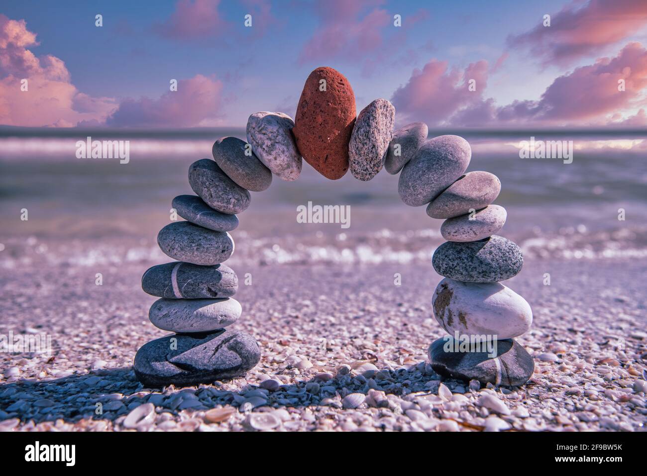 Side view of a stone arch with red stone at the top on a rocky beach ...