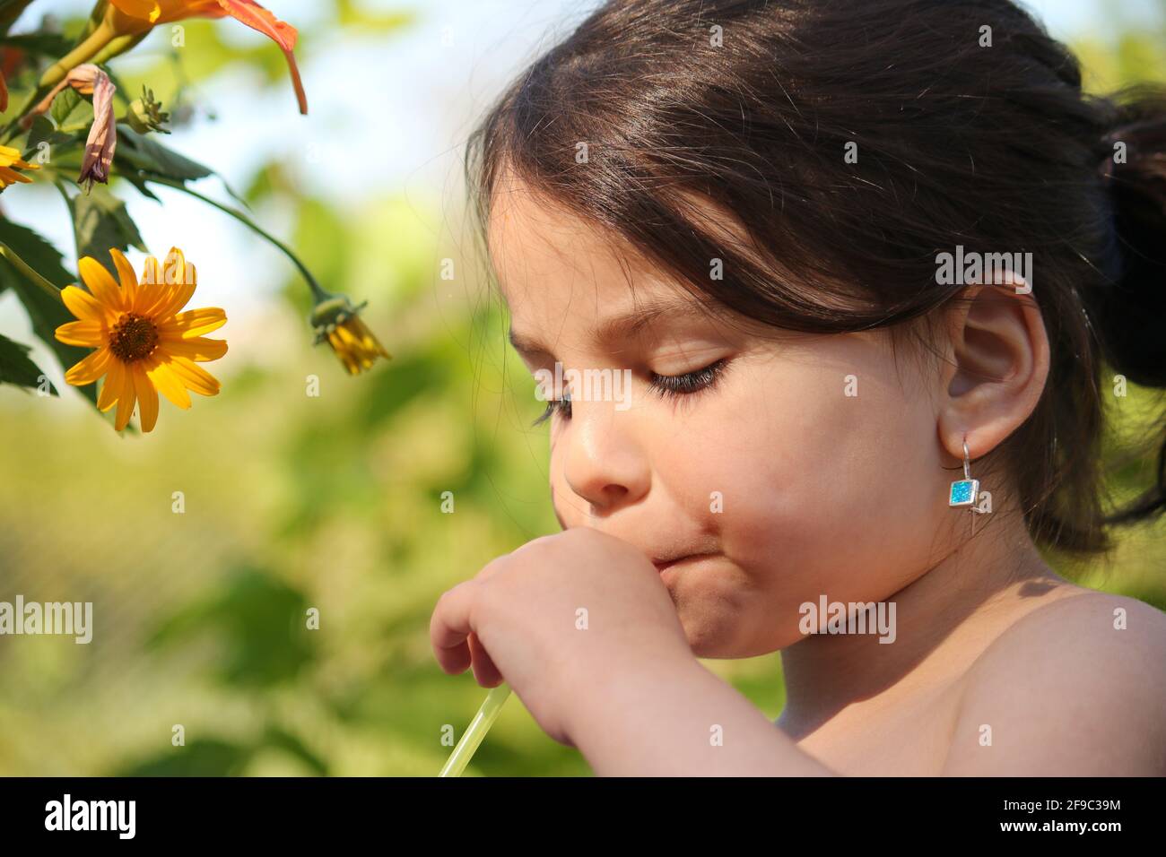 Adorable little girl drinks water through a straw from a plastic cup ...