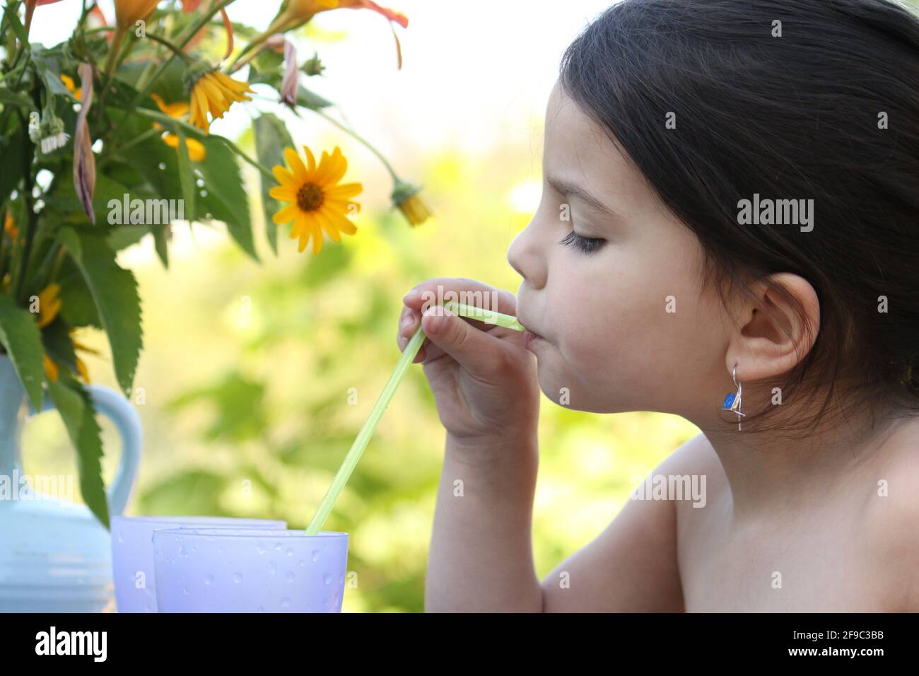 Summer vacation in the village. Little girl drinks water from a glass ...