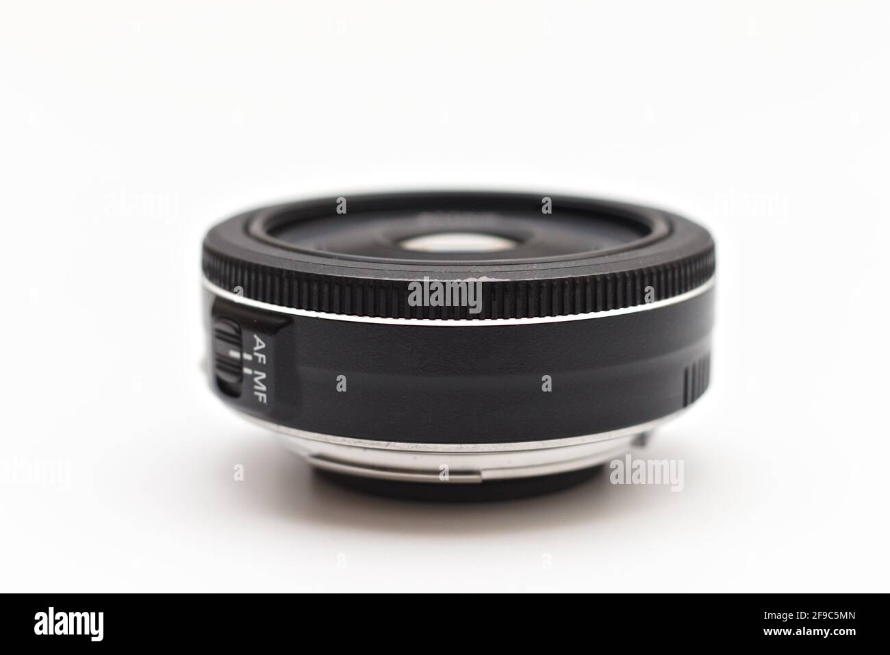 A small black 24mm lens with no name for a DSLR camera lying on a white ...